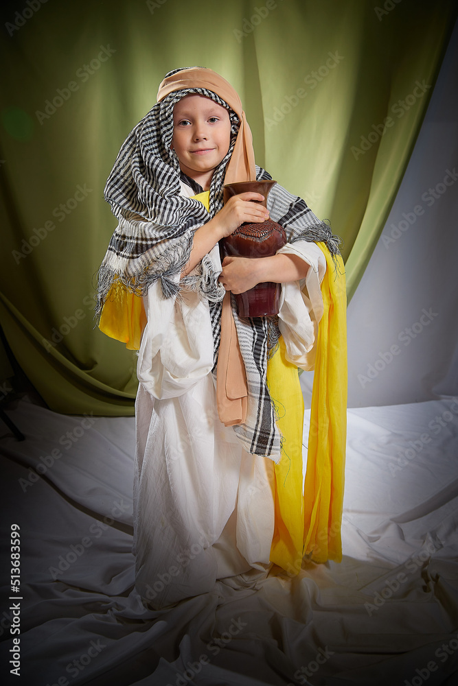 Little funny boy in long white and yellow dress with scarf on head and ...
