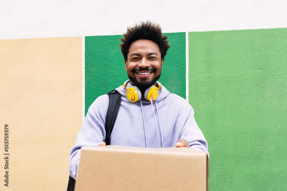 Smiling delivery man giving box standing in front of colorful wall ...