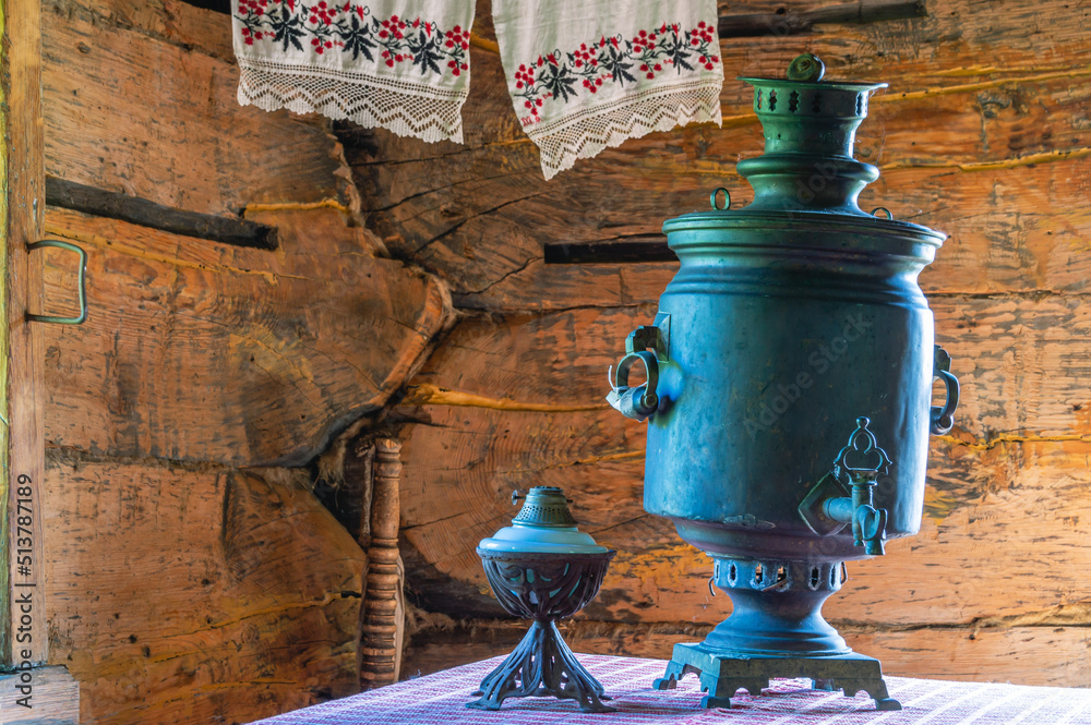 An old dark samovar and an oil lamp on a table in a rustic log house ...