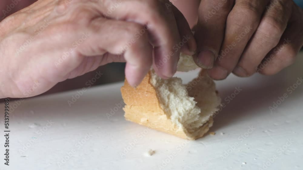 close-up of the hands of an elderly man breaking a piece of white bread ...