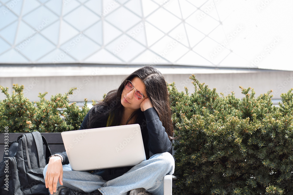 Young bored girl student sitting on city street bench using laptop ...