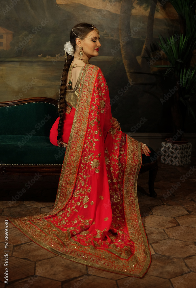 Charming woman is sitting on the sofa. Traditional Indian wedding sari ...