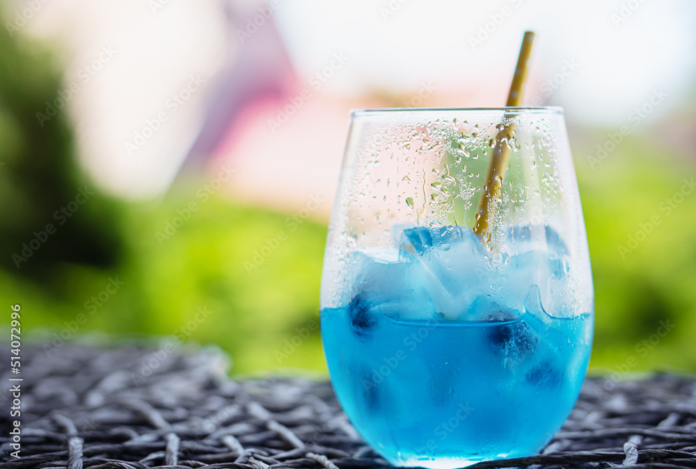 Glass of tasty blue cocktail and yellow lemons on blured background ...