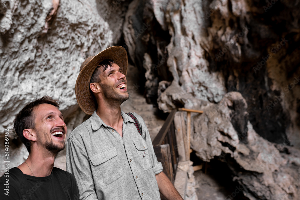 Two young friends wearing a hat are having fun exploring a cave and ...