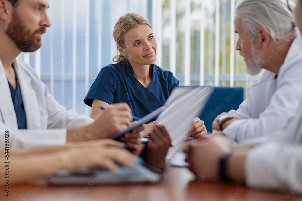Group of doctors sitting at meeting table in conference room during ...