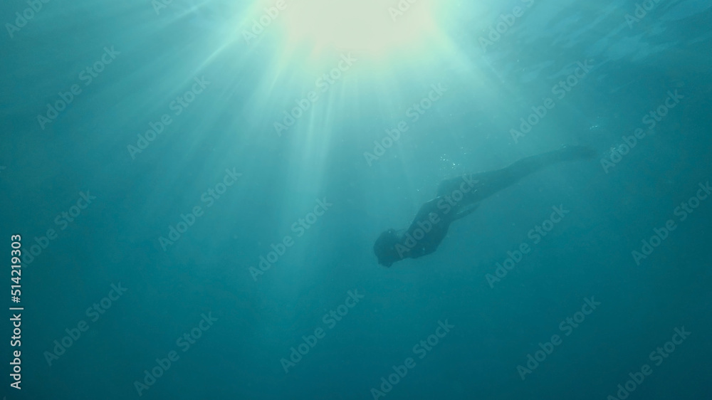 Silhouette of free diver woman swimming in deep blue sea on breath hold ...