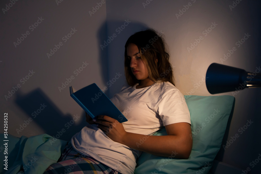 Teen girl in her room lying on her bed reading some notes at night with ...