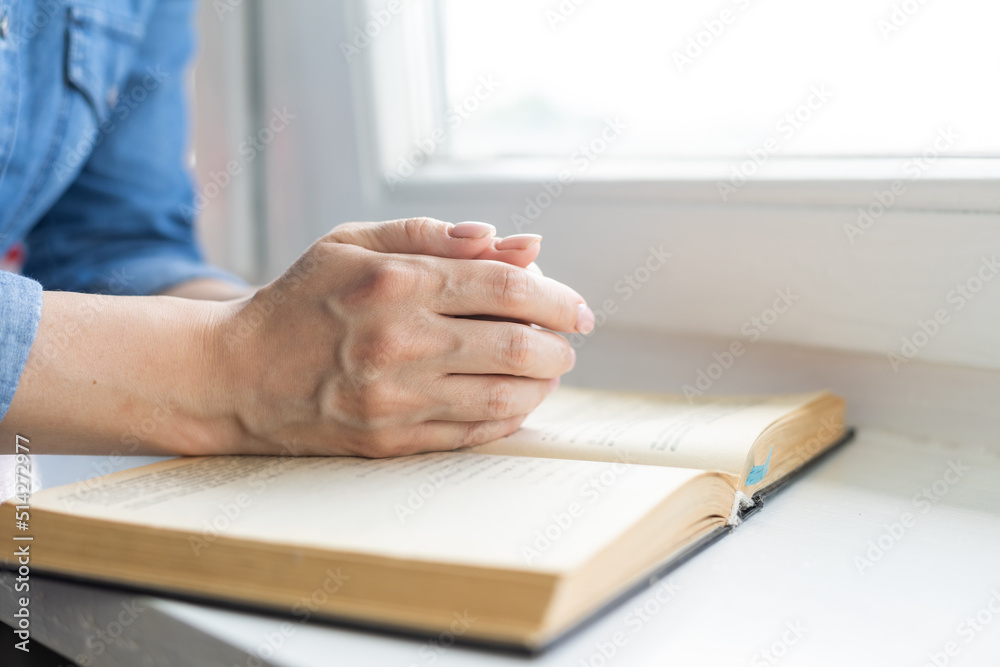 Hands folded in prayer on a Holy Bible for faith, spirituality and ...