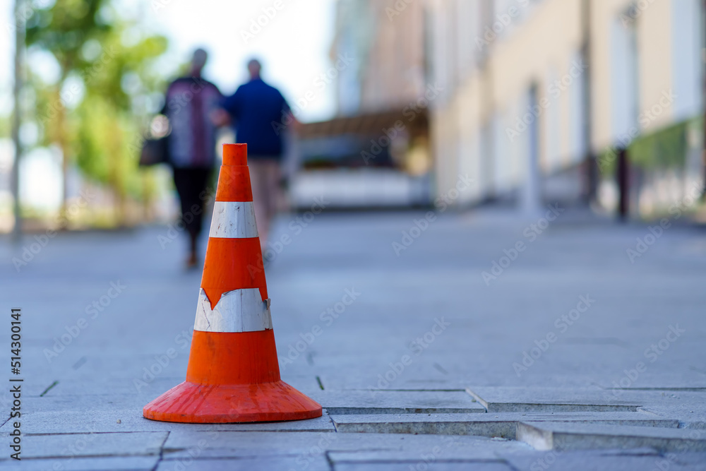 Protective cone behind which are silhouettes of two people walking side ...