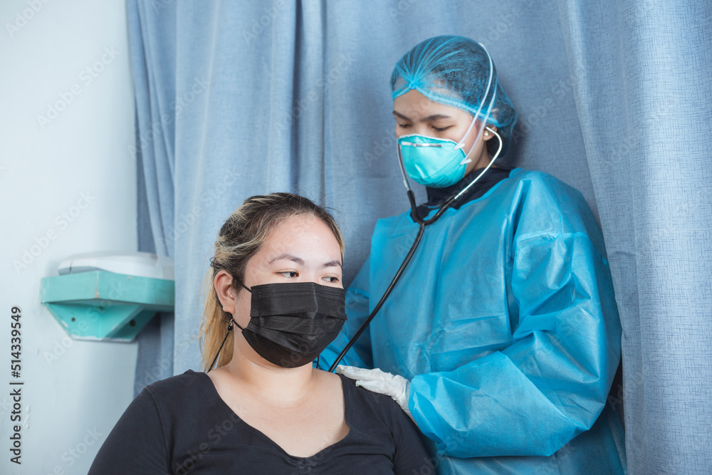 A doctor in full PPE gear checks a patient's breathing with a ...