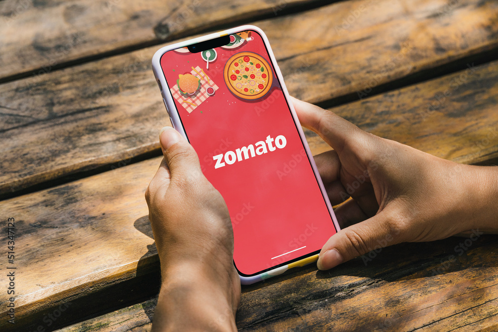 Girl in the park holding a smartphone with Zomato food delivery app on ...