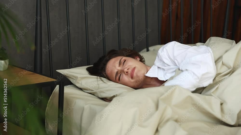Sad tired young woman wears casual white shirt she lying in bed spend ...