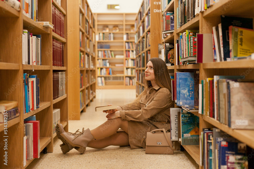 Young woman sitting at the library holding book. millennial reading ...