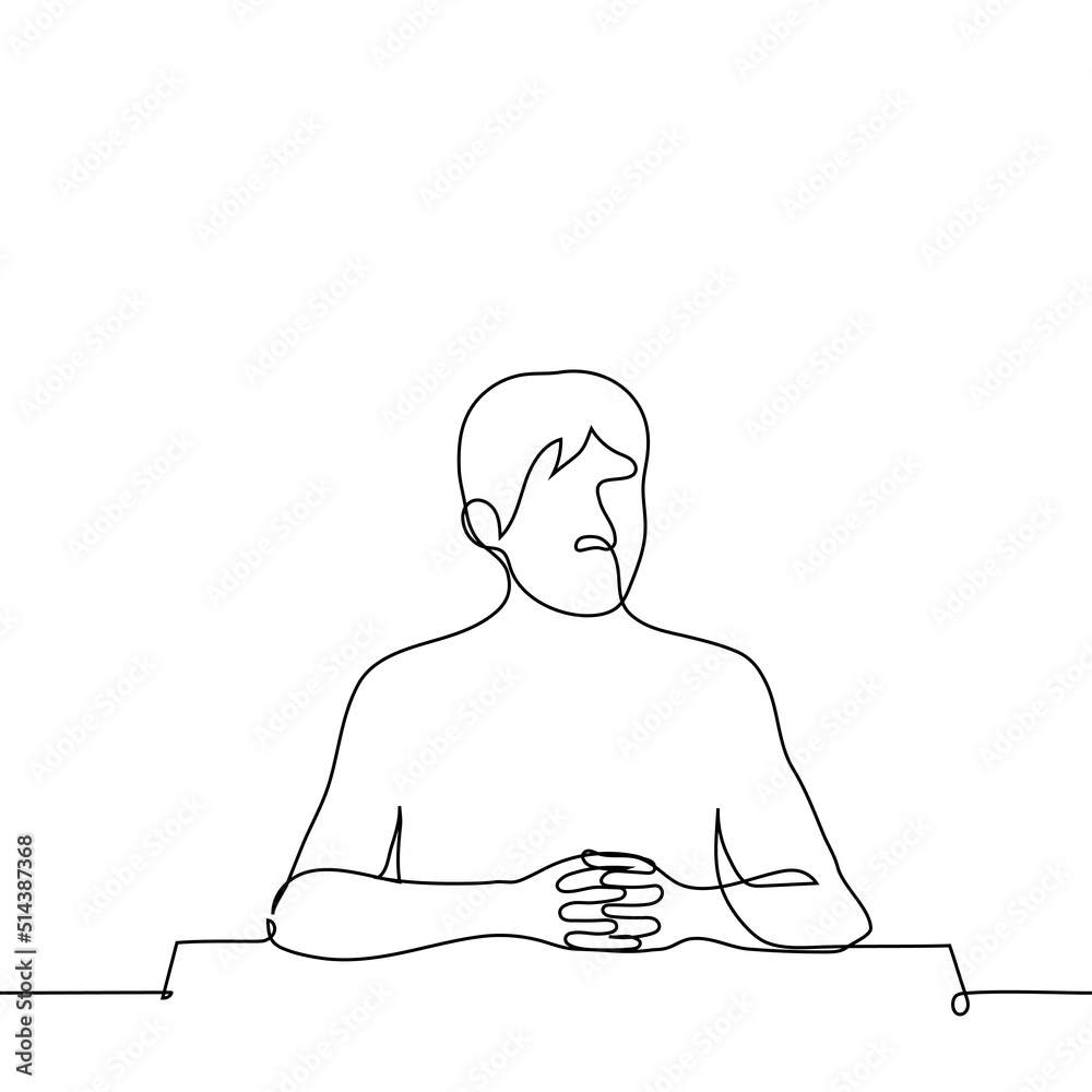 man diligently sitting at the table with his hands clasped together ...