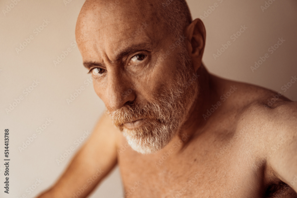 Bald man with bare torso and unkempt beard looks with serious ...