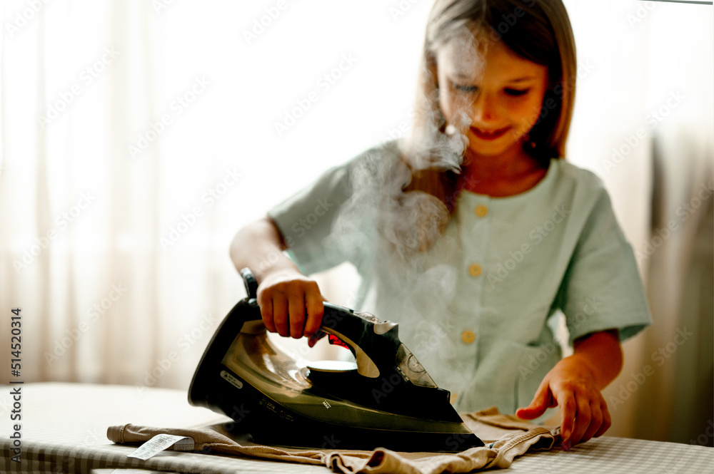A 6-7-year-old girl helps her mother around the house, she irons ...