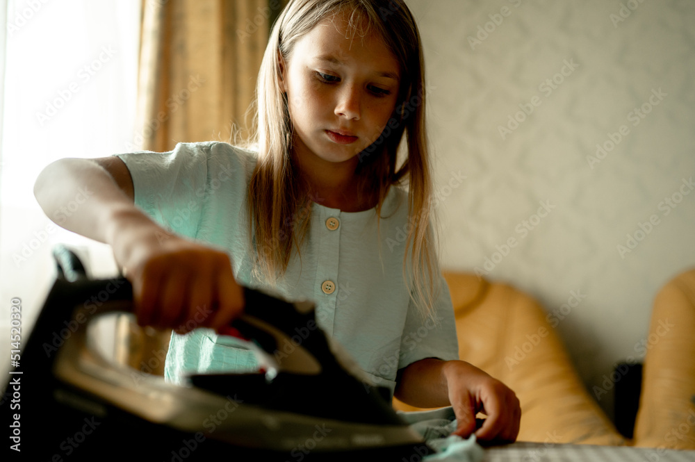 A 6-7-year-old girl helps her mother around the house, she irons ...