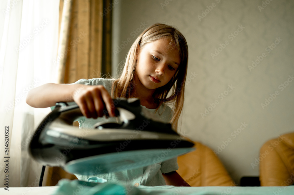 A 6-7-year-old girl helps her mother around the house, she irons ...