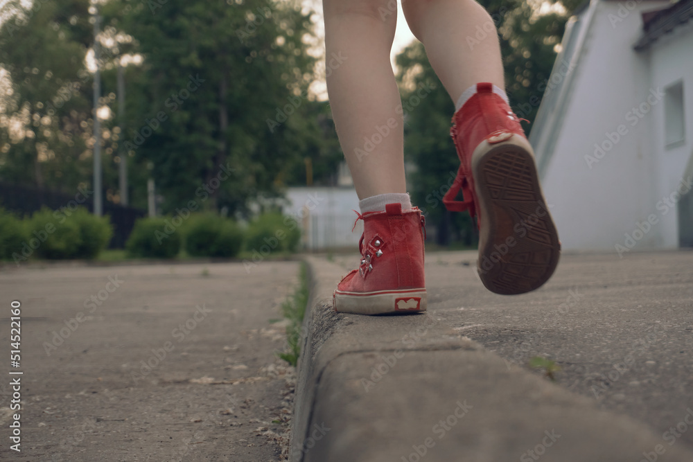 Girl child in red sneakers walks on the curb, Development of the ...