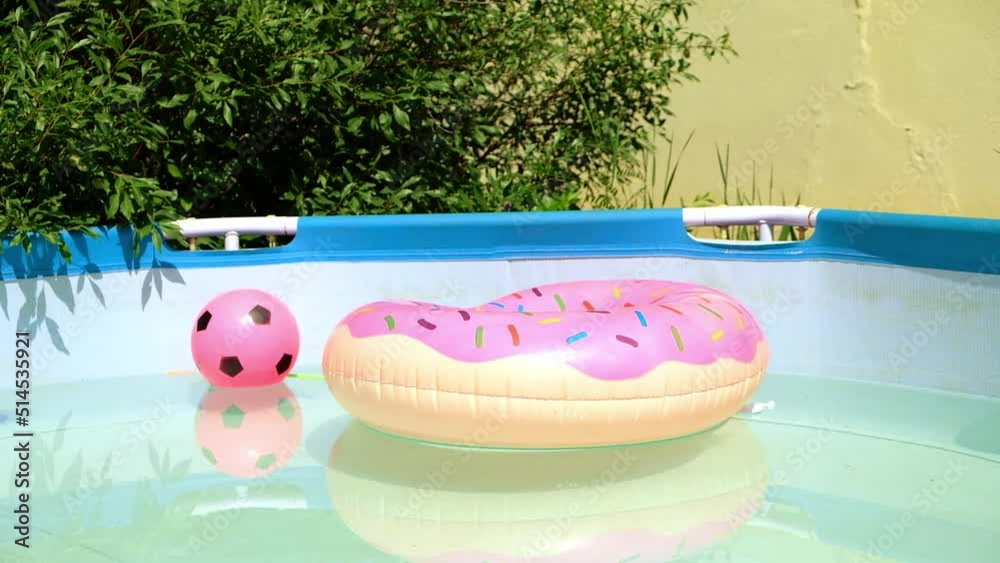Children swimming pool, pink ball and donut float on sunny summer day ...