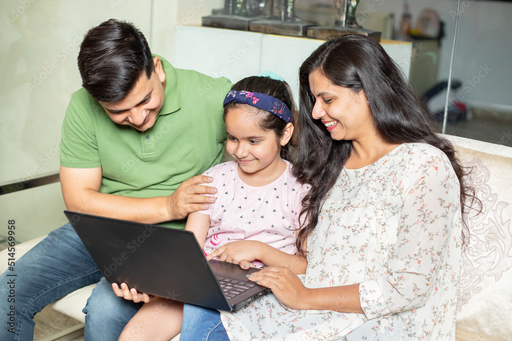 Young Indian parents teach daughter how to use laptop computer at home ...