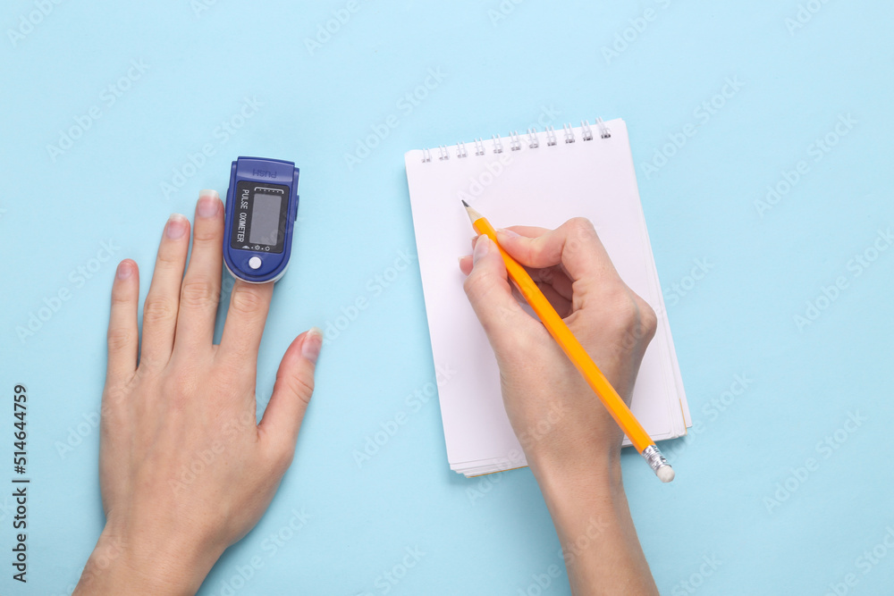 Hand finger with a pulse oximeter and hand writing data in a notebook ...
