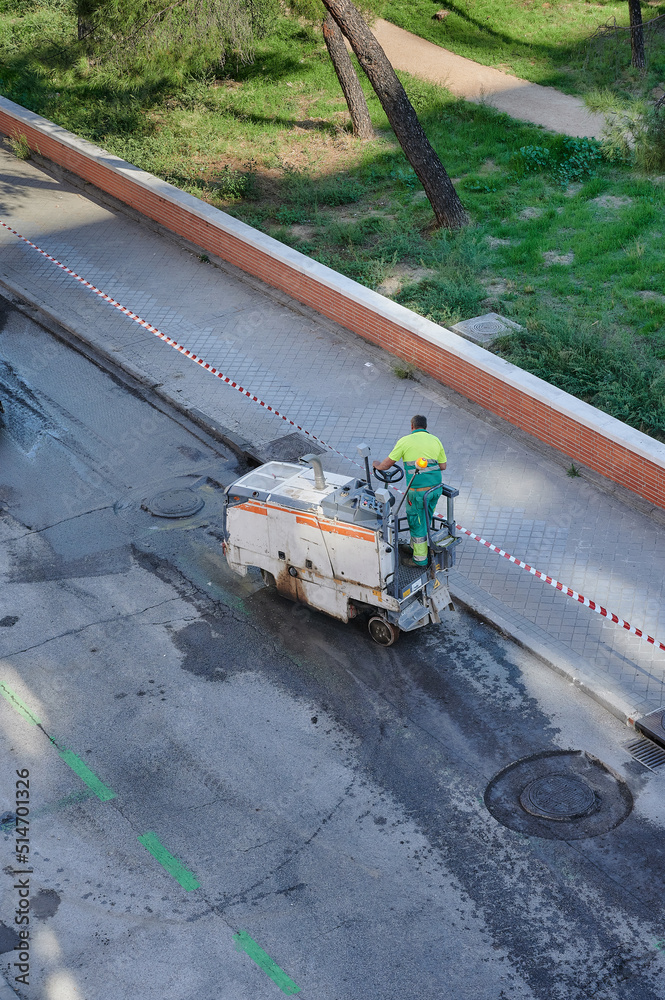 Small milling asphalt machine driven by a worker in a street while a ...