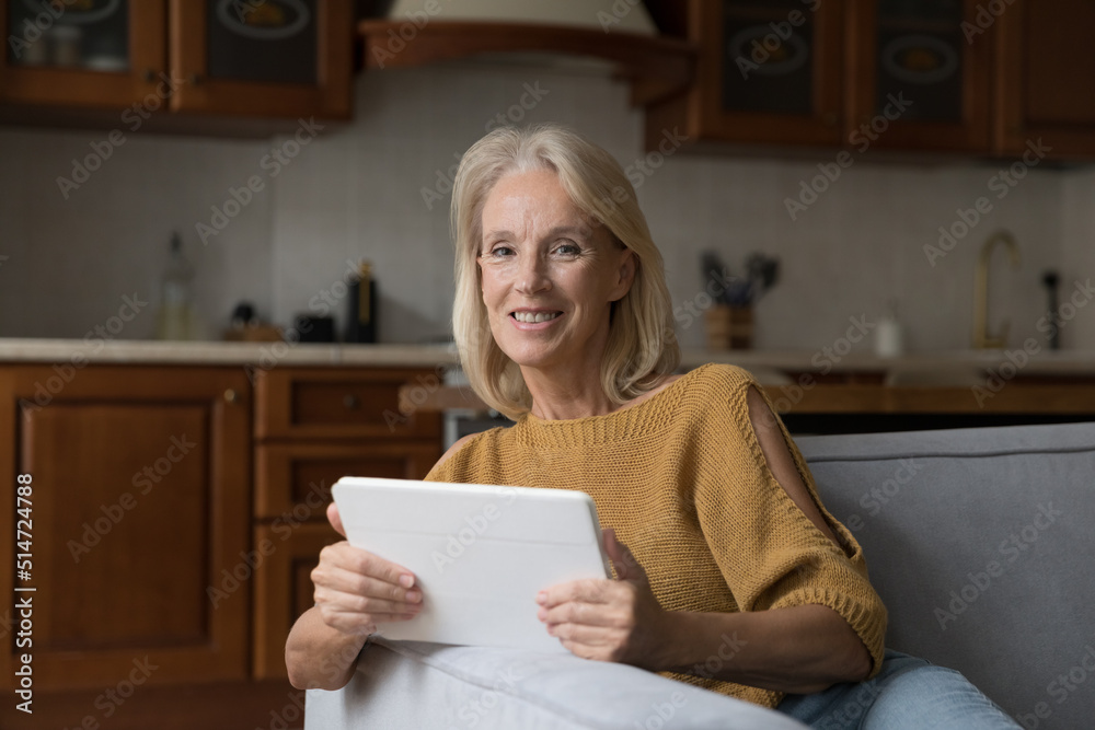 Good-looking blonde senior woman use digital tablet at home, sit on ...