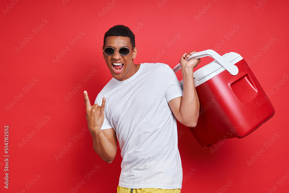 Excited African man carrying cooler box and gesturing while standing ...