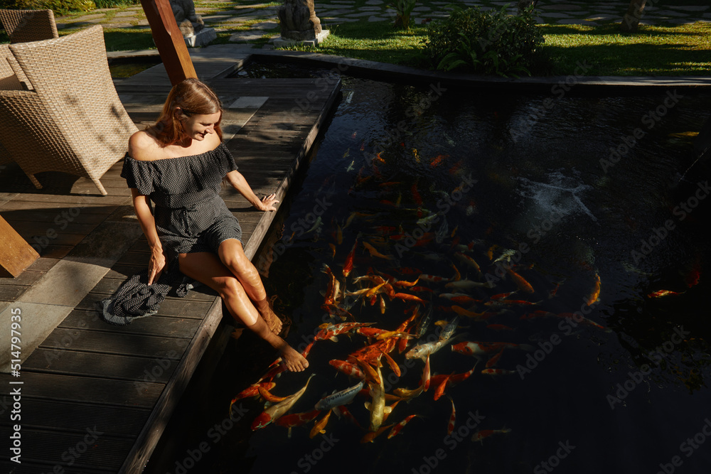 Girl feeds the fish by hand in a small pond in the yard. Koi fish ...