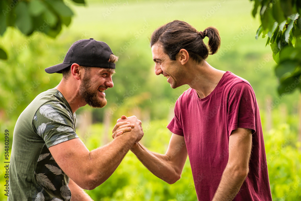 two male brothers shake hands smiling in natural background, dressed in ...