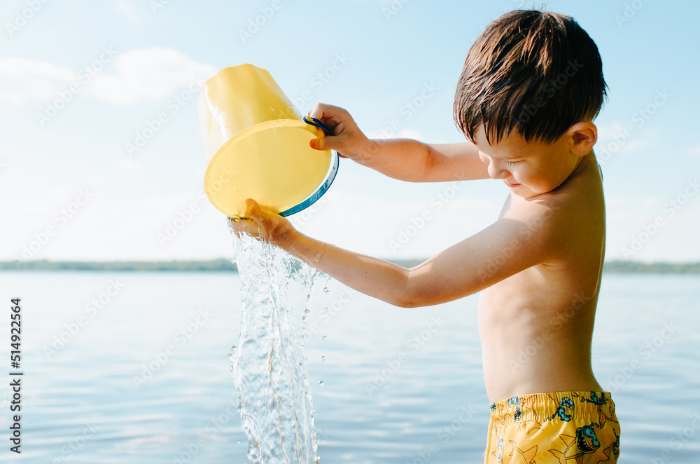 Boy playing in water in nature. Child pouring water from bucket while ...
