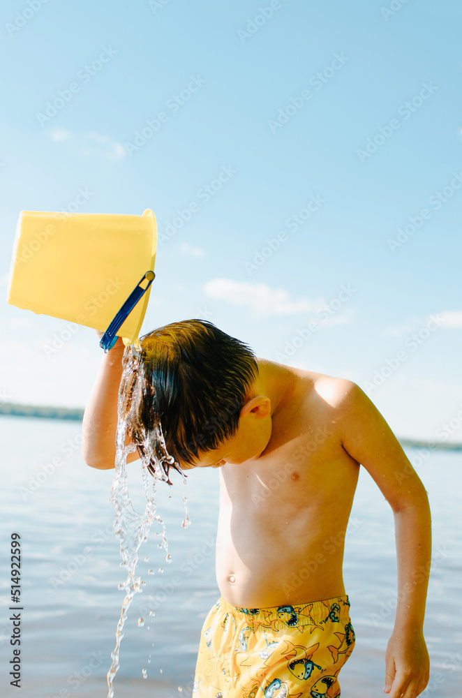 Boy playing in lake, pouring water from bucket in hot summer weather ...