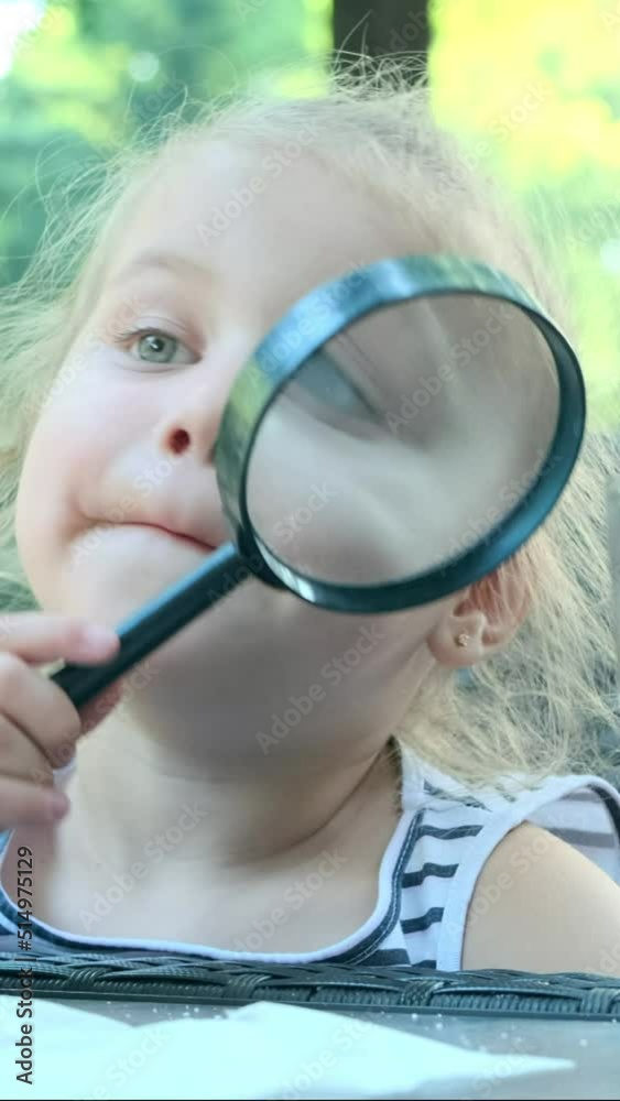 VERTICAL VIDEO: Little girl looks into the lens into the lens and ...