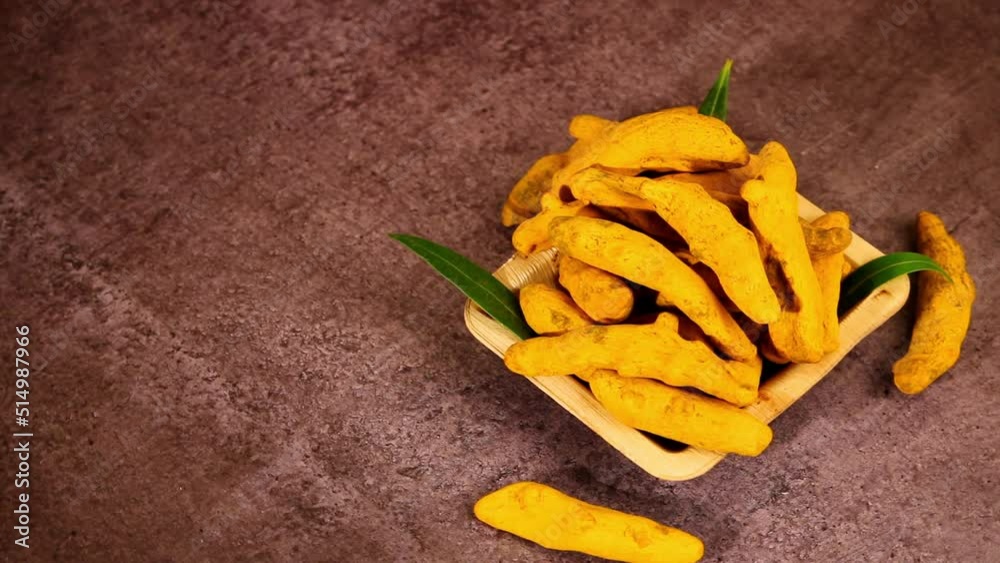 whole turmeric fingers or sticks in a bowl with green leaves on wooden ...