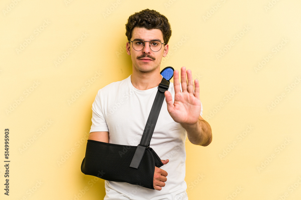 Young caucasian man with broke hand isolated on yellow background ...
