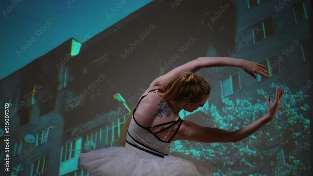 Tattooed talented graceful ballerina bending back looking at camera performing at background of ...