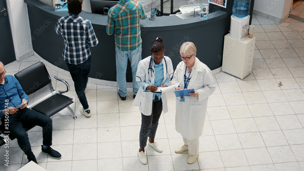 Diverse medical team of doctors talking and writing report in hospital ...