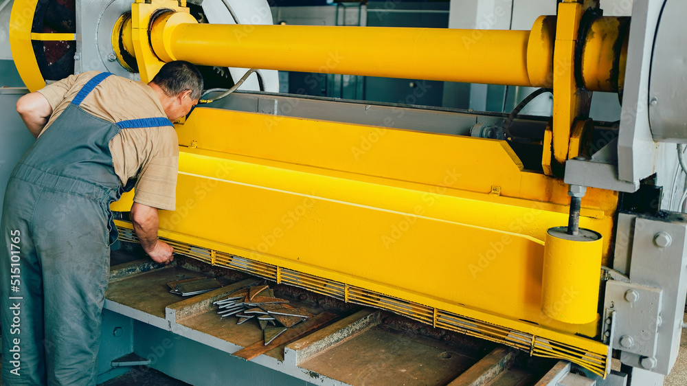 Foto de Worker cuts metal sheets on mechanical guillotine machine in ...