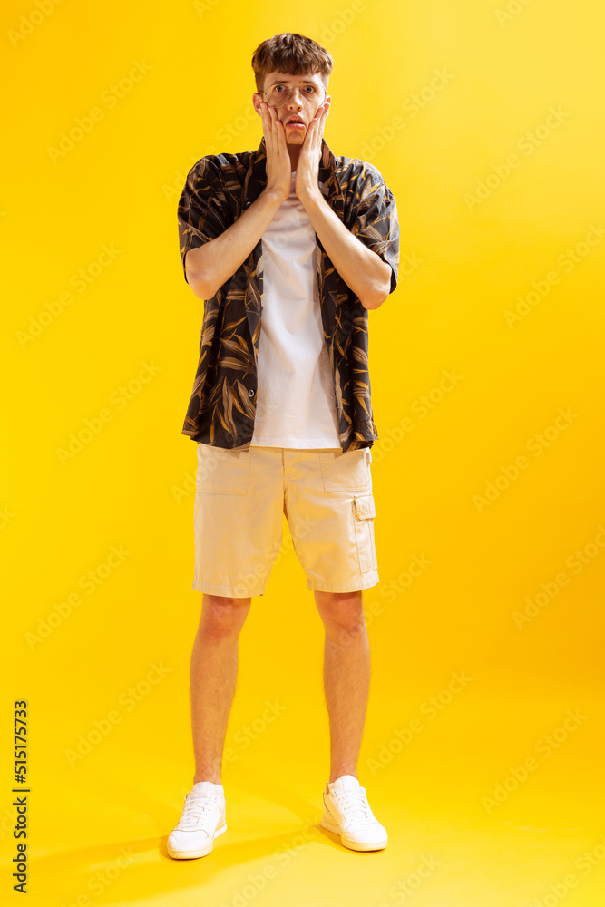 Scared young man, teen in short and shirt standing isolated on bright ...
