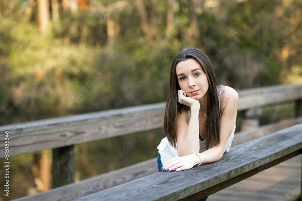 A tall and thin brunette teenager standing and leaning on a park bridge ...