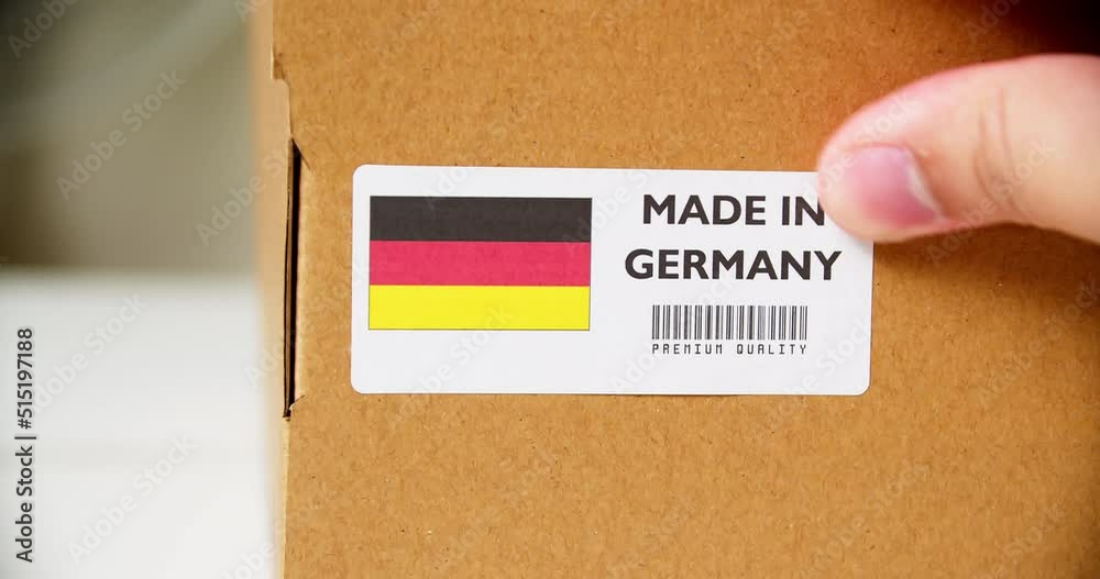 Hands applying MADE IN GERMANY flag label on a shipping cardboard box ...