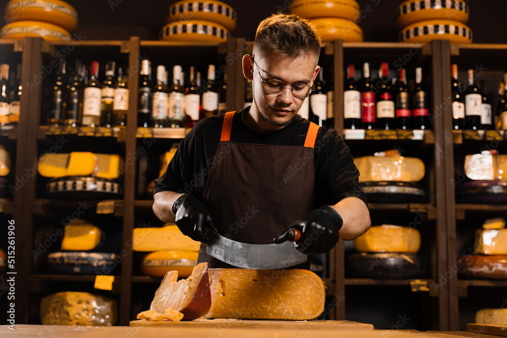 Handsome man worker of cheese shop cut limited gouda with knife. Cheese ...