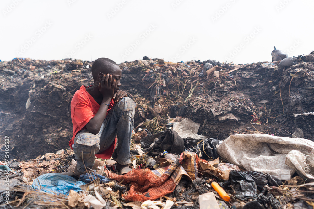 Poor African slum boy sitting in front of a large pile of garbage in ...