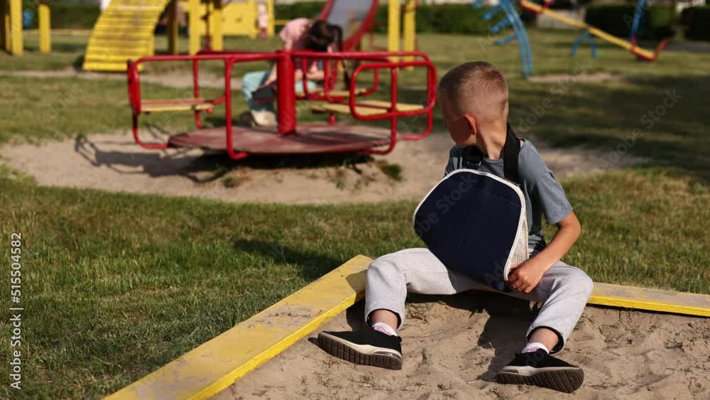 crying child with broken limb arm sits outdoors and looking how kid ...