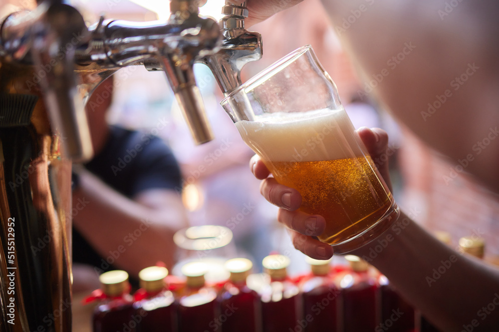 bartender hand at beer tap pouring a draught beer in glass serving in a ...