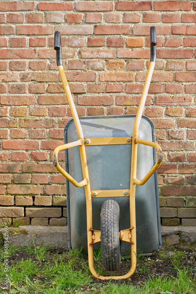 Garden wheelbarrow leaning against a red brick wall in a home backyard ...