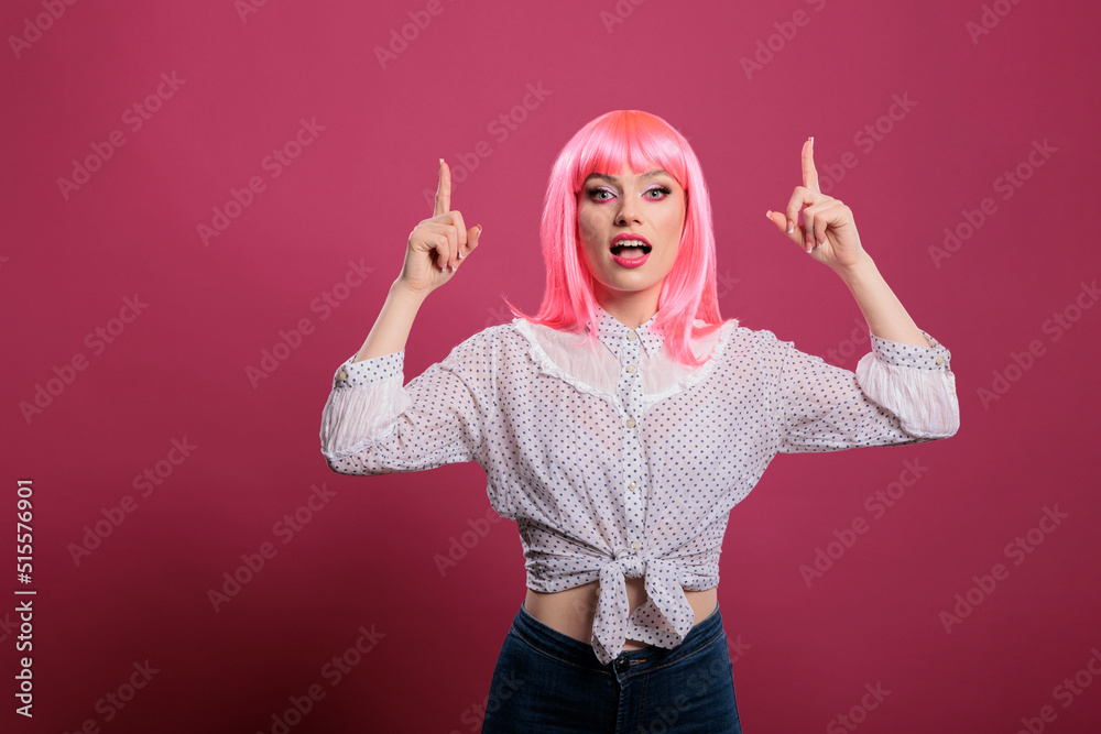 Smiling casual lady pointing up with index fingers in studio, posing ...