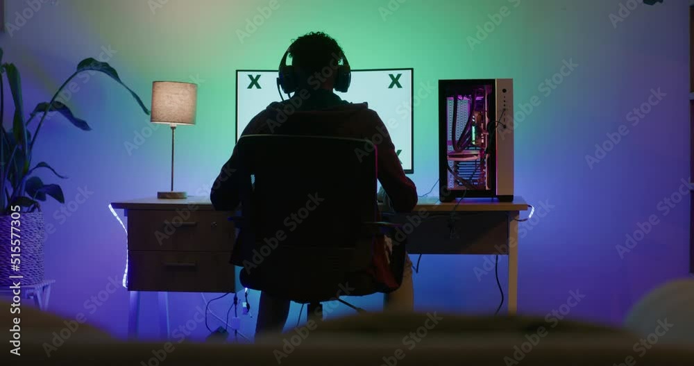 Back view of computer gamer wearing headphones and playing pc games ...