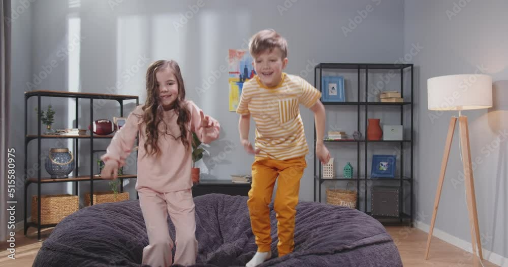 Caucasian small cute kids, boy and girl jumping on soft round sofa and ...